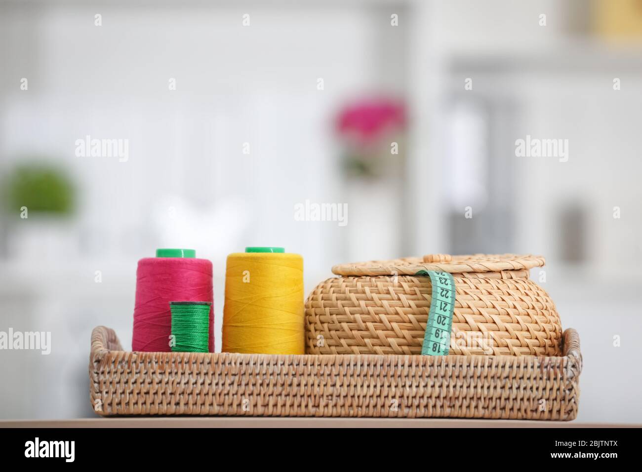 Spools of colorful threads and box with sewing accessories in wicker ...
