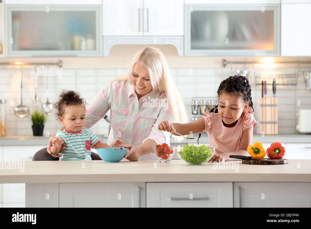 Female mature nanny with little African-American sisters in kitchen ...
