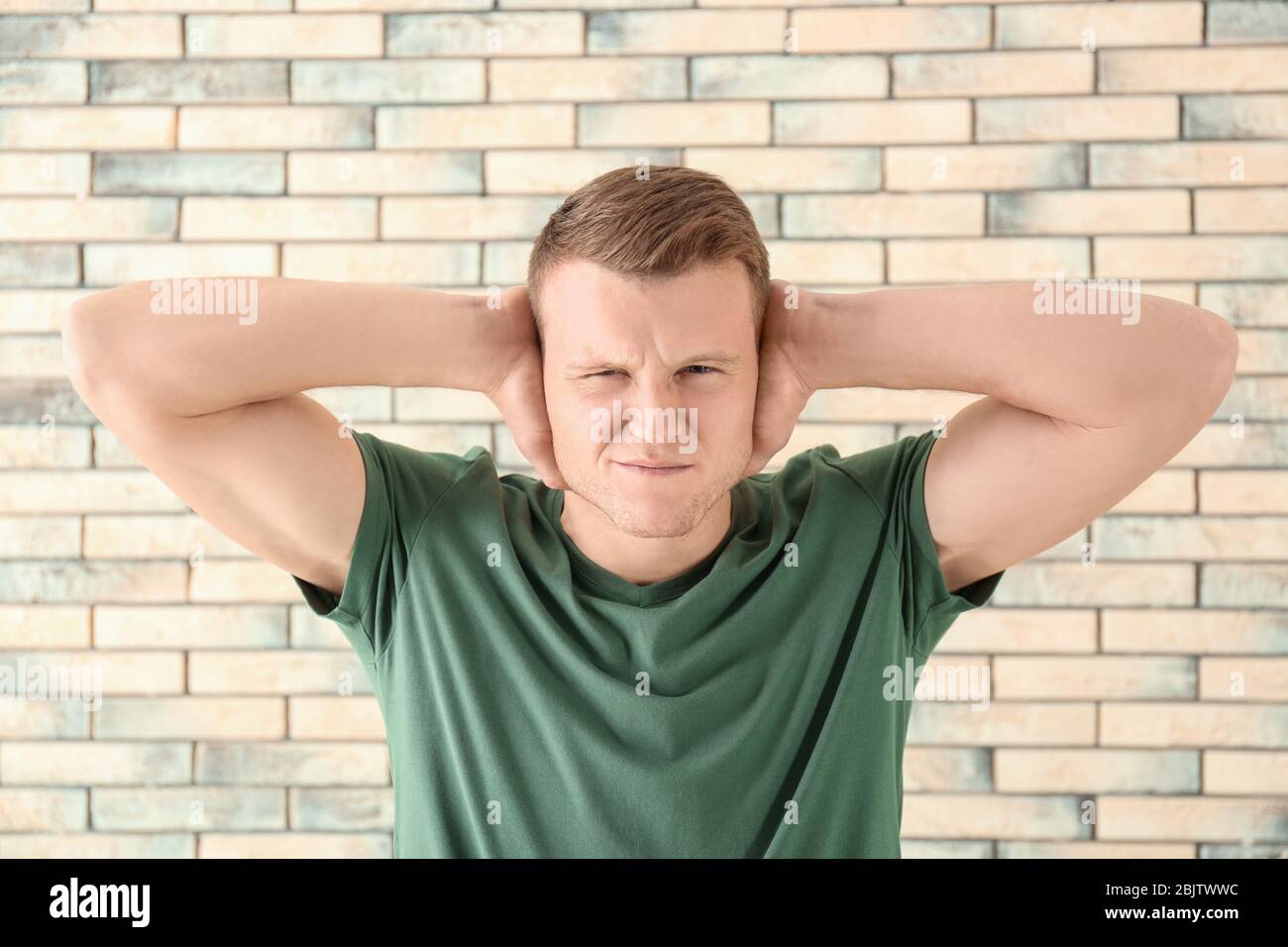 Man covering his ears on brick wall background. Hearing problem Stock ...