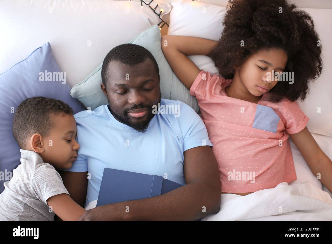 African American man sleeping with his children in bed. Family bedtime ...