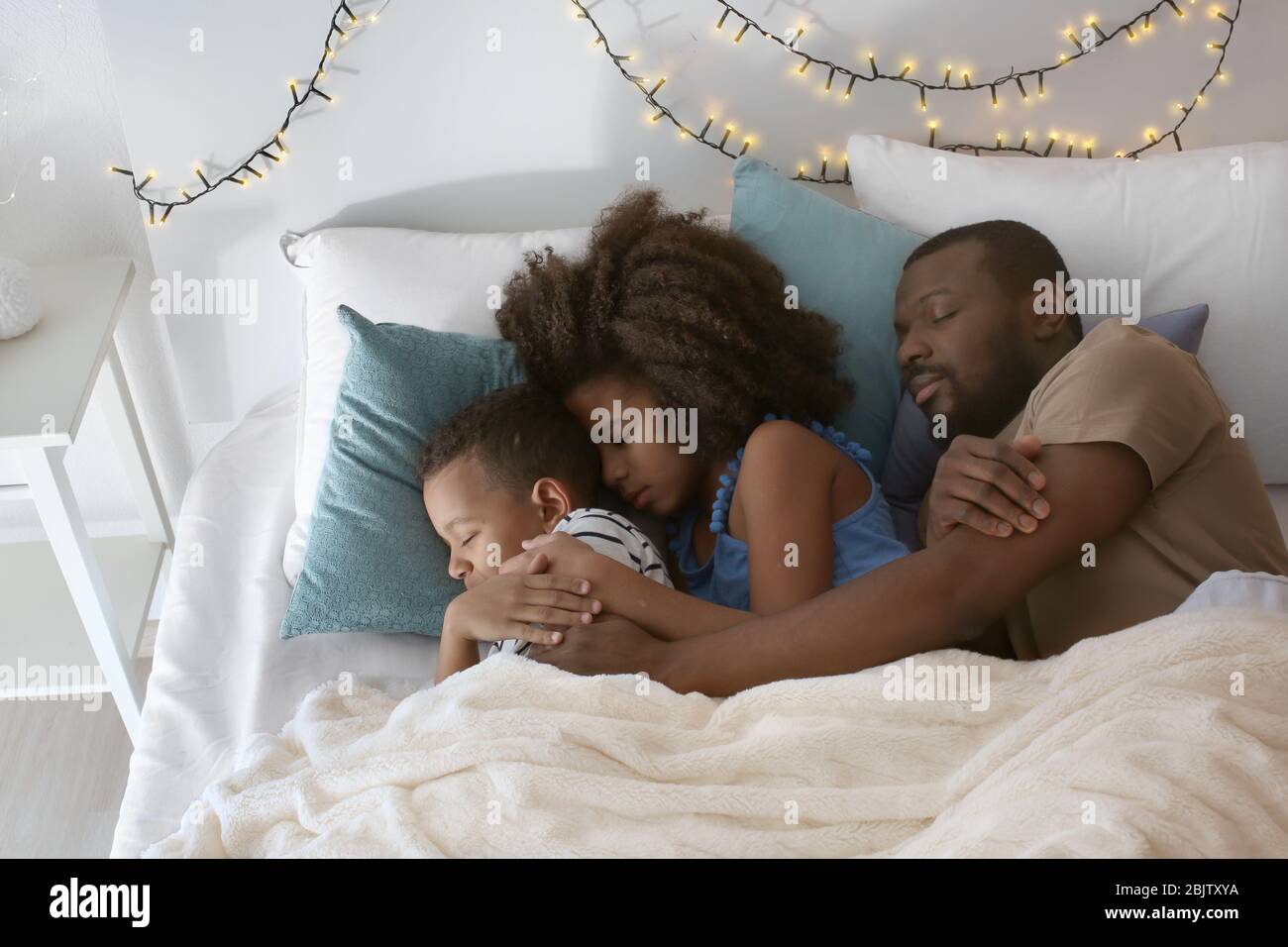 African American man sleeping with his children in bed. Family bedtime ...