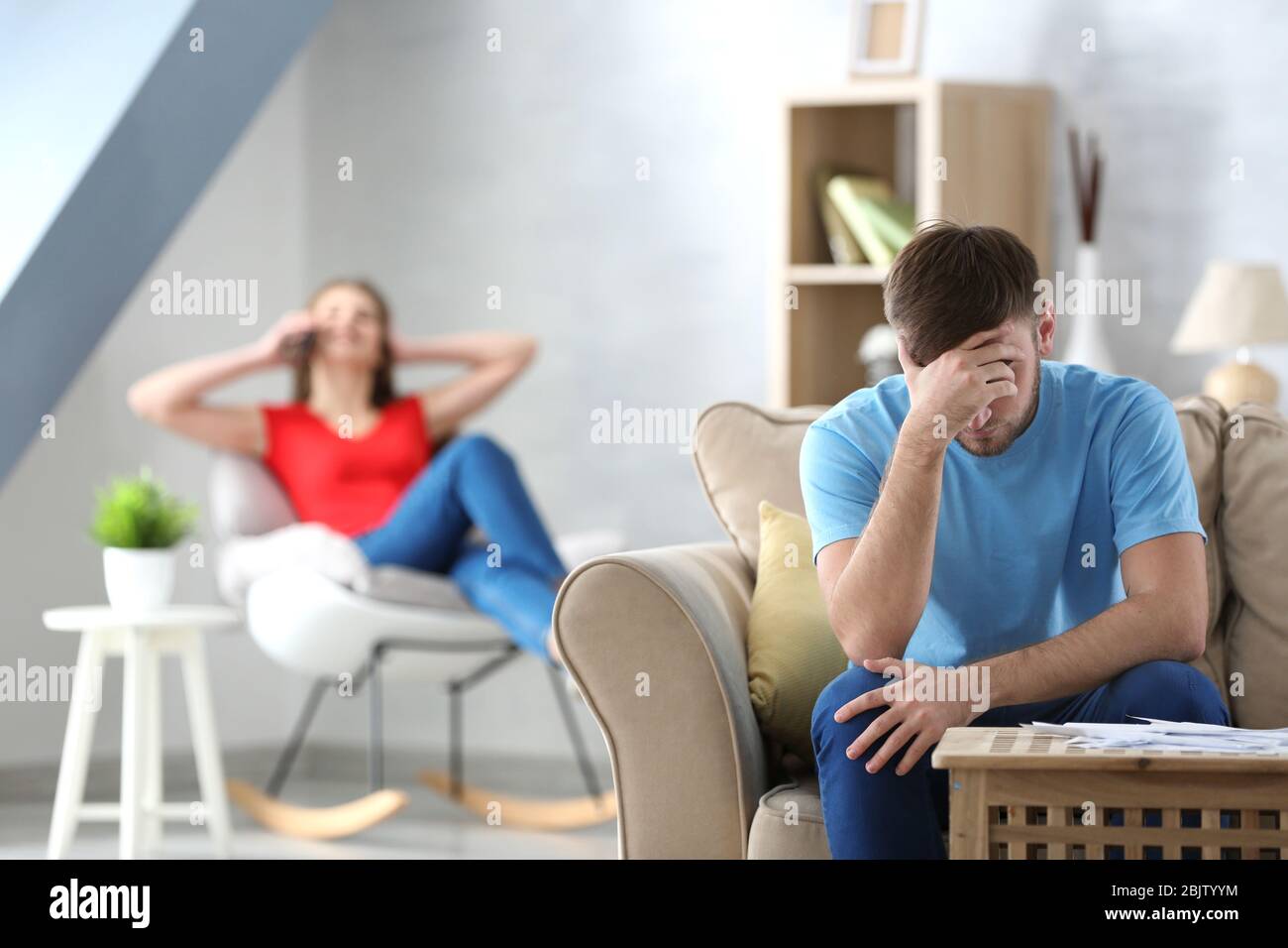 Sad man at table with bills and blurred woman on background. Money ...