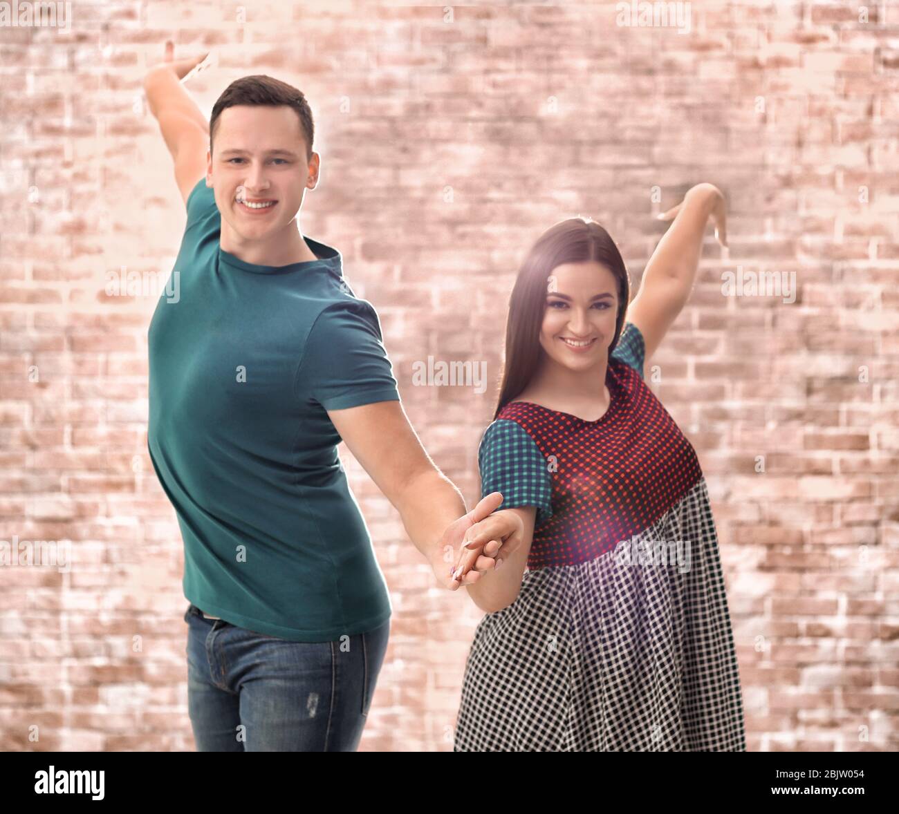 Happy young couple dancing against brick wall Stock Photo - Alamy