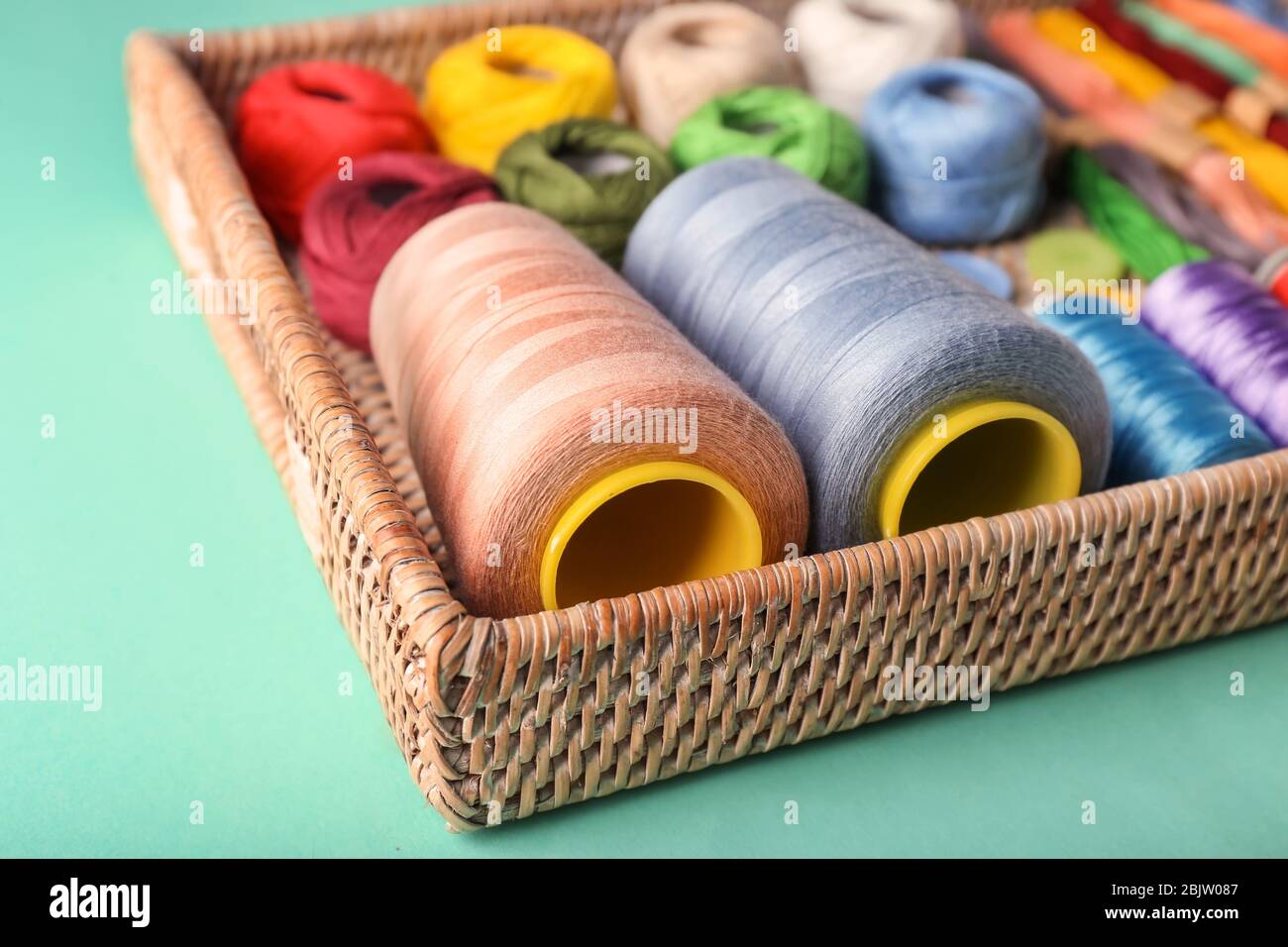 Wicker tray with sewing threads on color background, closeup Stock ...