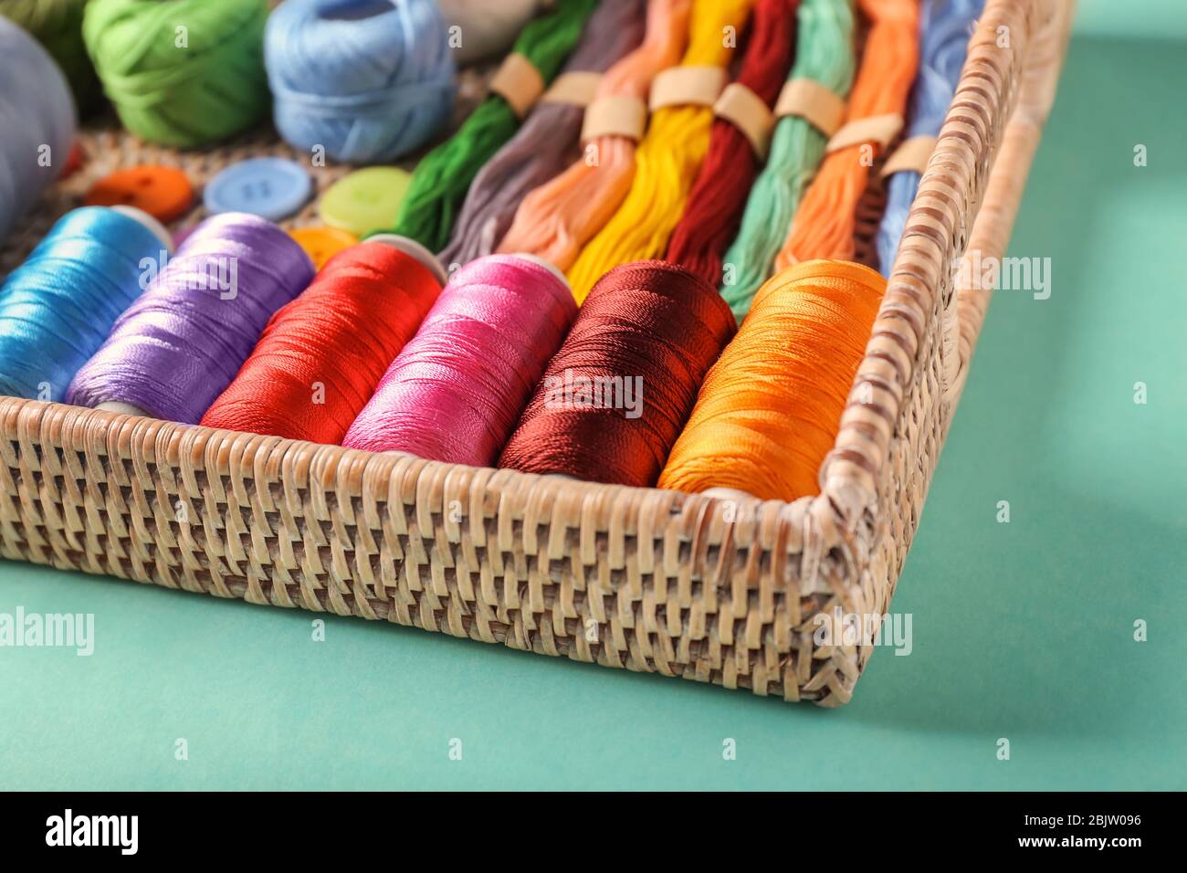 Wicker tray with different types of threads on color background ...
