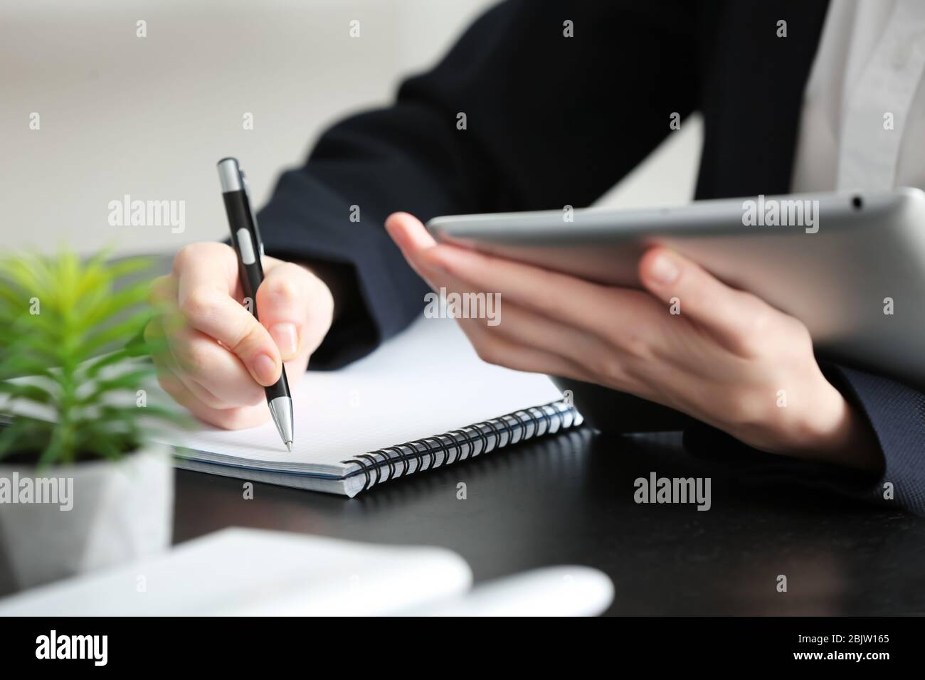 Female student with tablet computer writing in notebook at table ...
