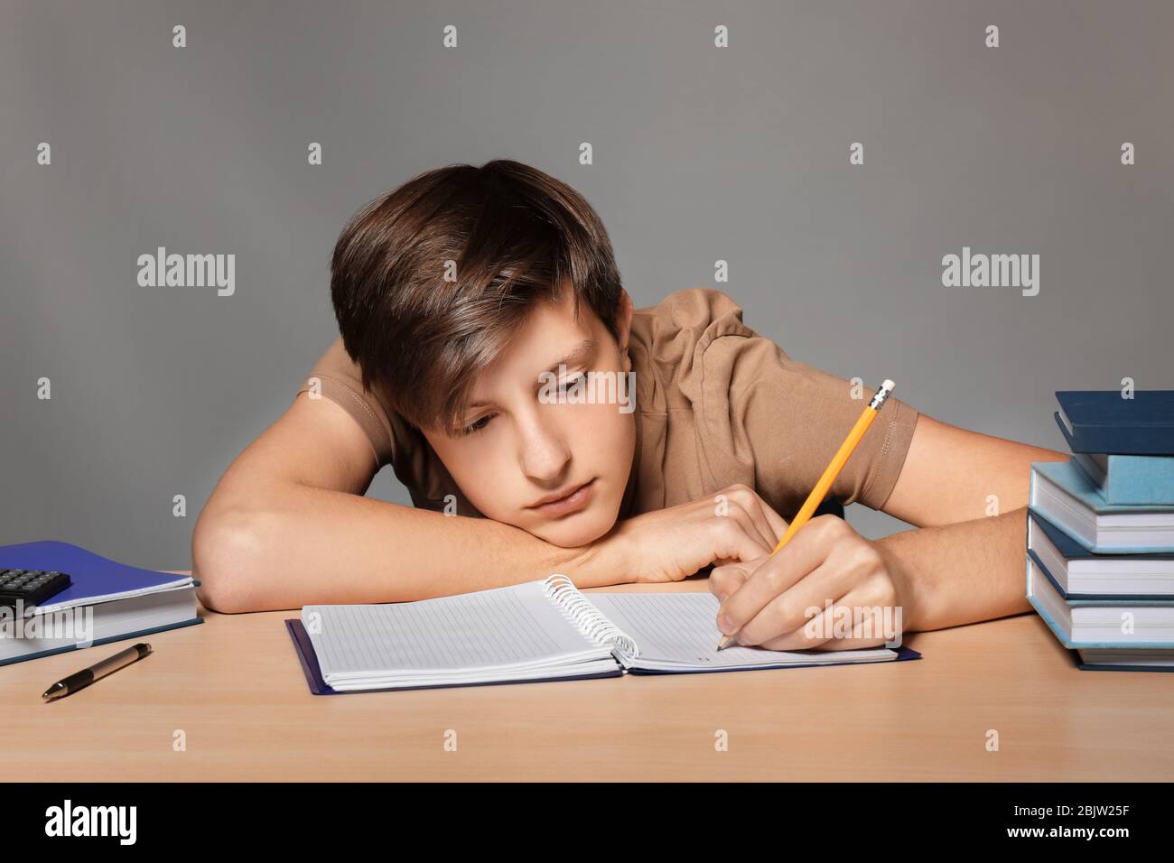 Tired teenager boy doing homework against grey background Stock Photo ...