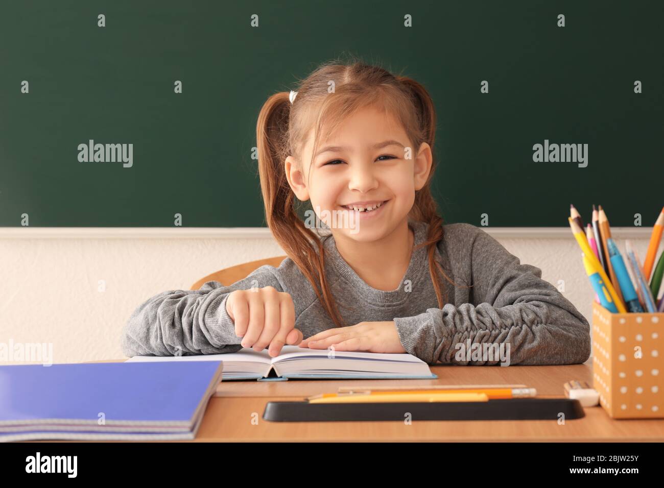 Cute little girl doing homework in classroom Stock Photo - Alamy