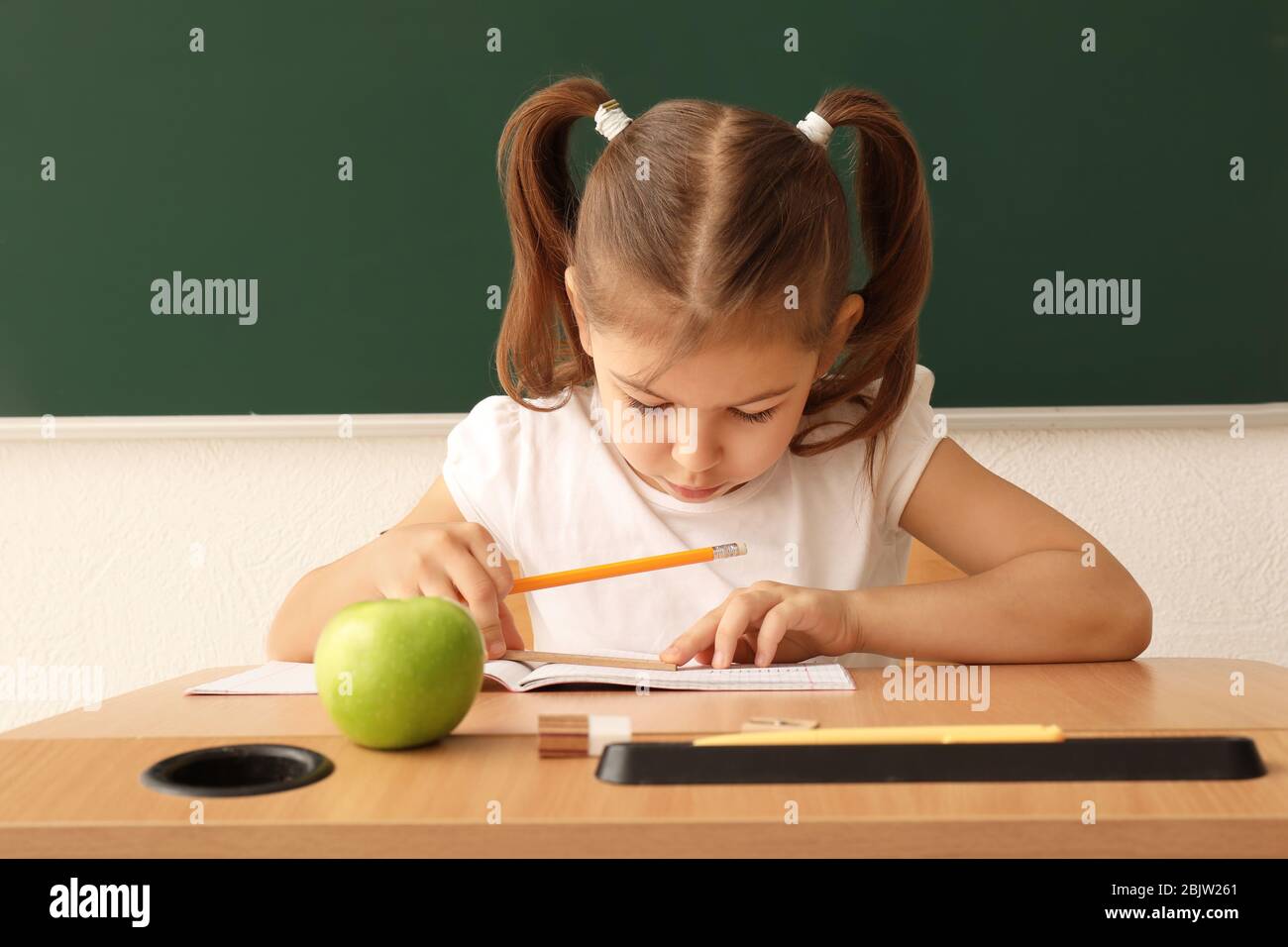 Cute little girl doing homework in classroom Stock Photo - Alamy