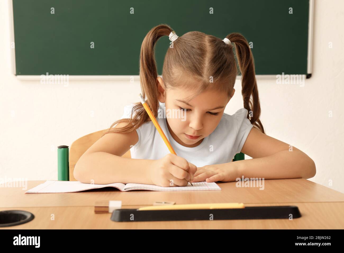 Cute little girl doing homework in classroom Stock Photo - Alamy
