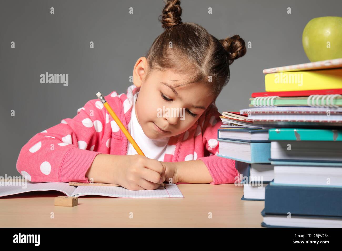 Cute little girl doing homework against grey background Stock Photo - Alamy