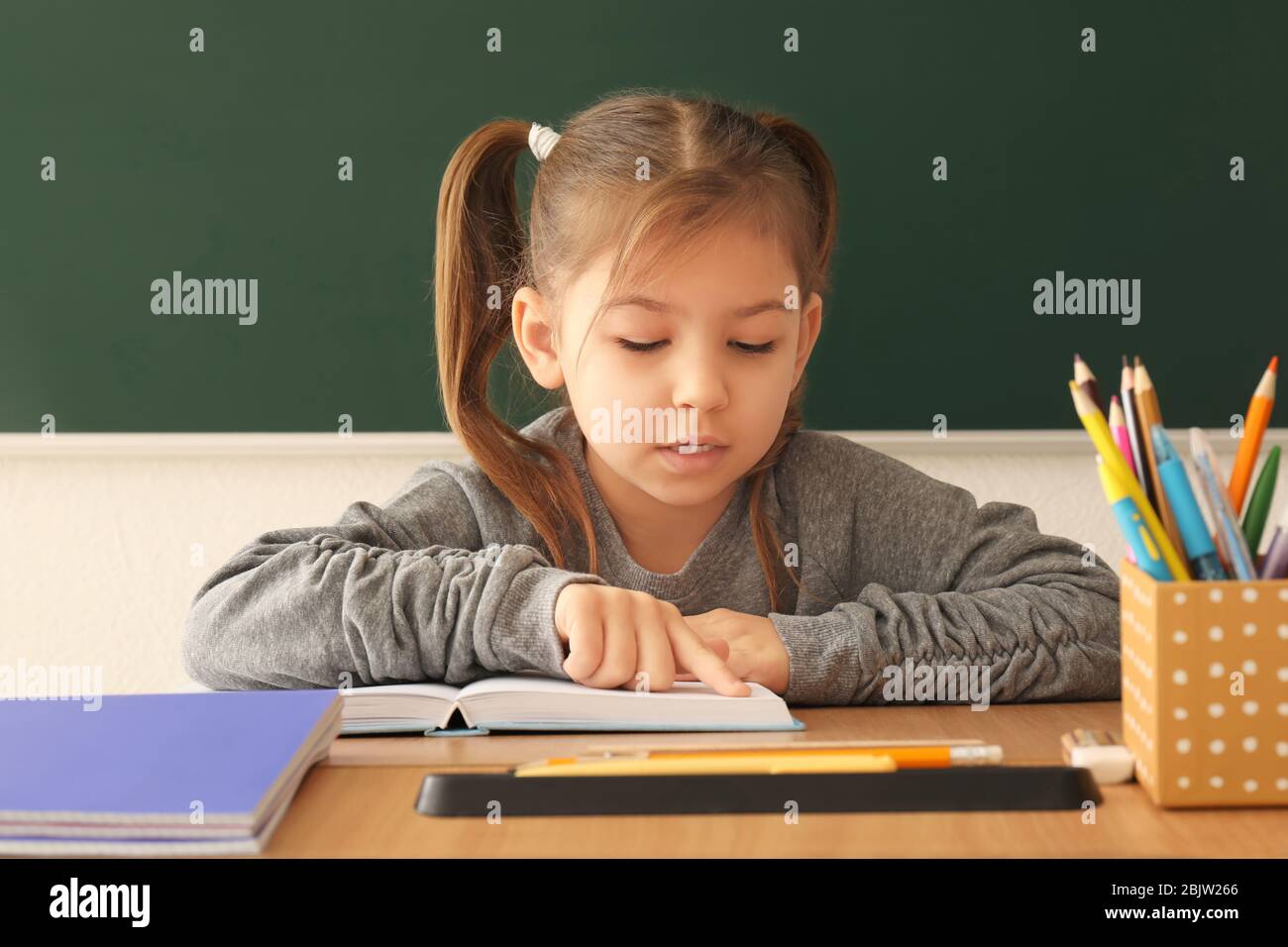 Cute little girl doing homework in classroom Stock Photo - Alamy