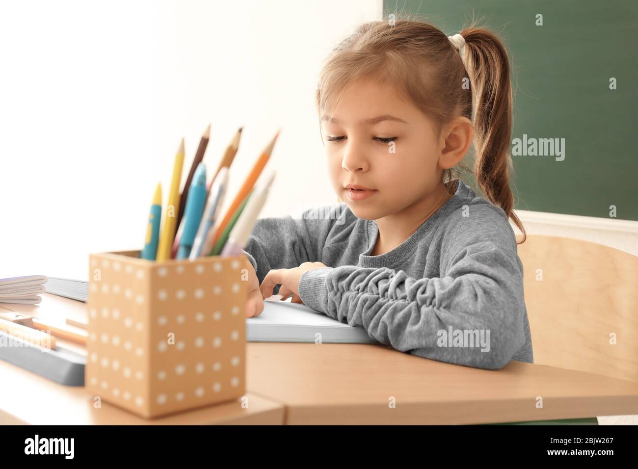 Cute little girl doing homework in classroom Stock Photo - Alamy