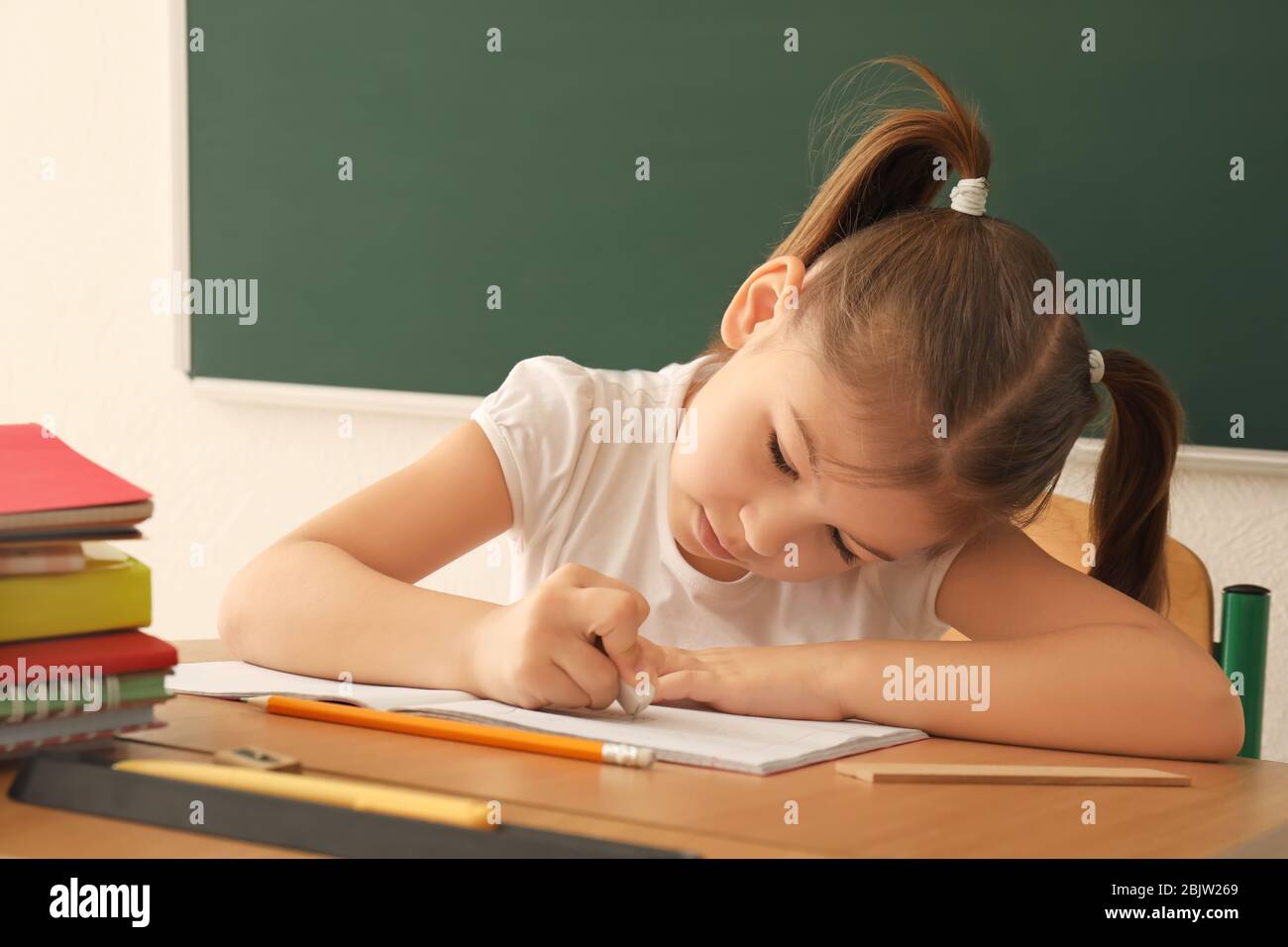 Cute little girl doing homework in classroom Stock Photo - Alamy