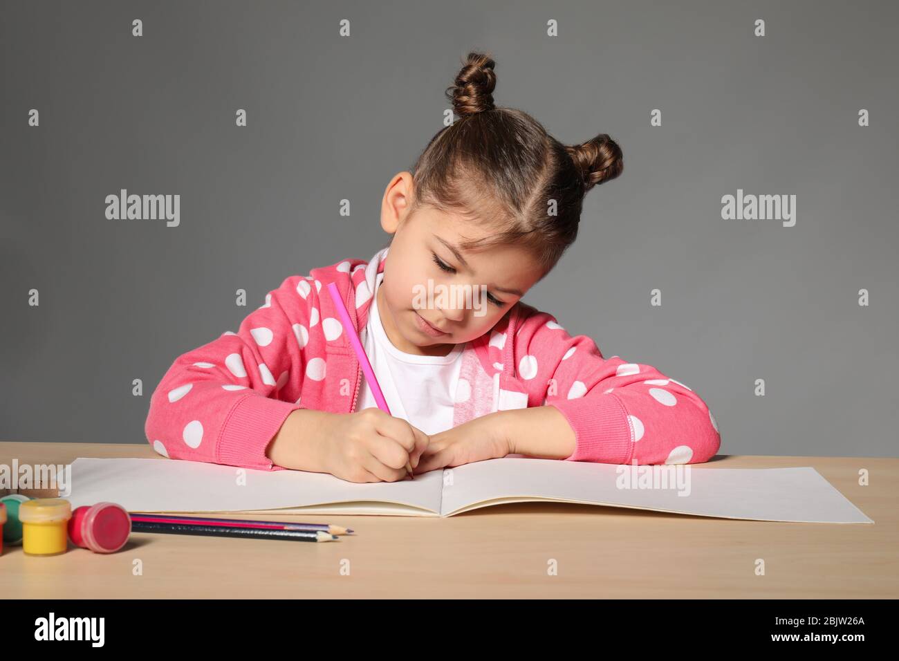 Cute little girl doing homework against grey background Stock Photo - Alamy