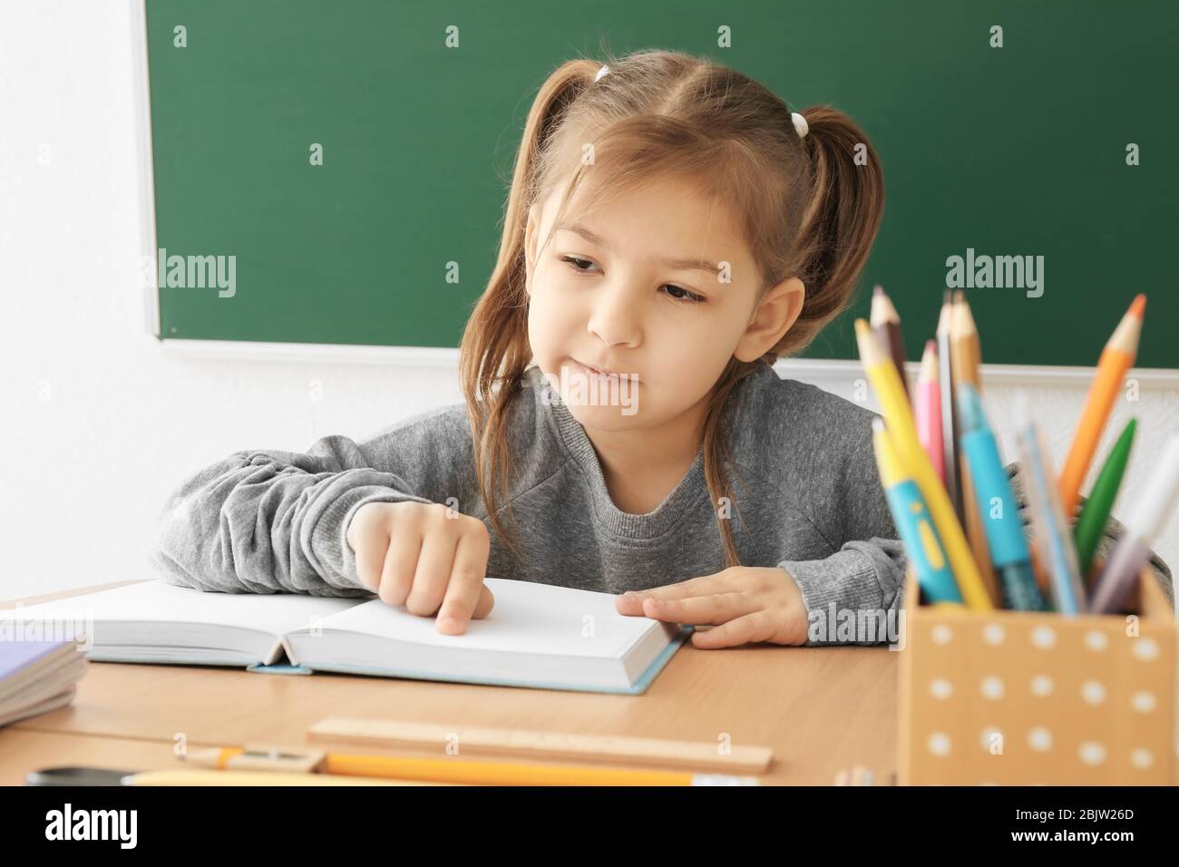 Cute little girl doing homework in classroom Stock Photo - Alamy