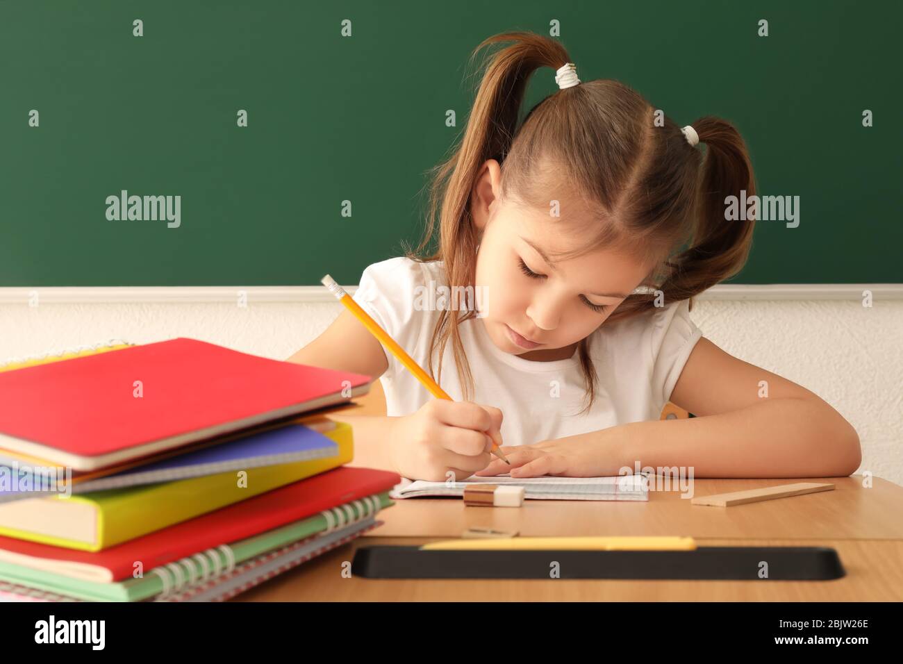 Cute little girl doing homework in classroom Stock Photo - Alamy