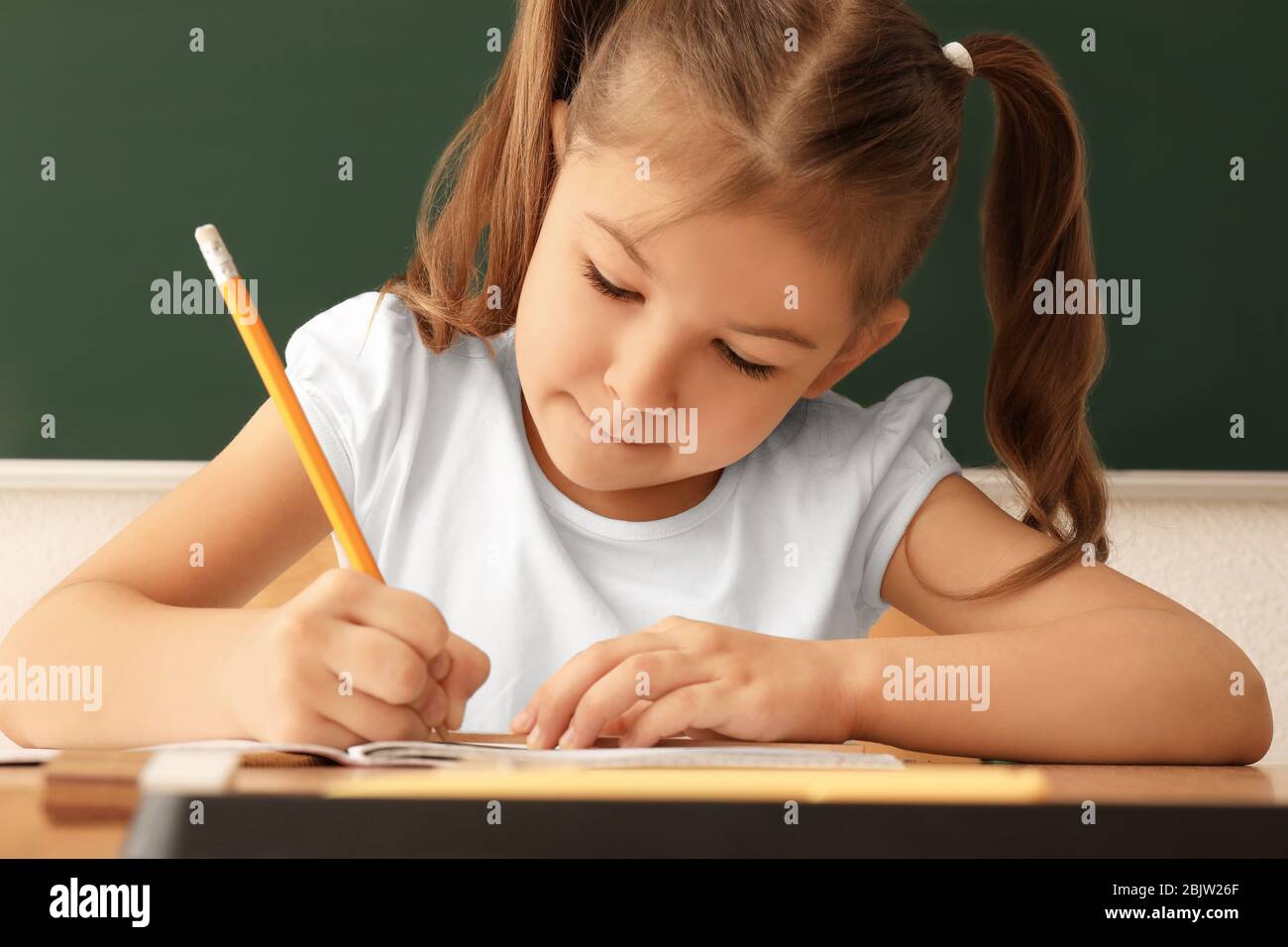 Cute little girl doing homework in classroom Stock Photo - Alamy