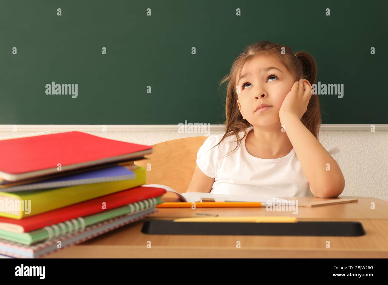 Thoughtful little girl doing homework in classroom Stock Photo - Alamy