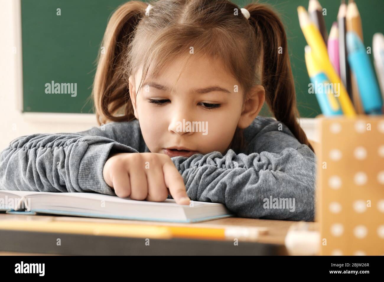 Cute little girl doing homework in classroom Stock Photo - Alamy