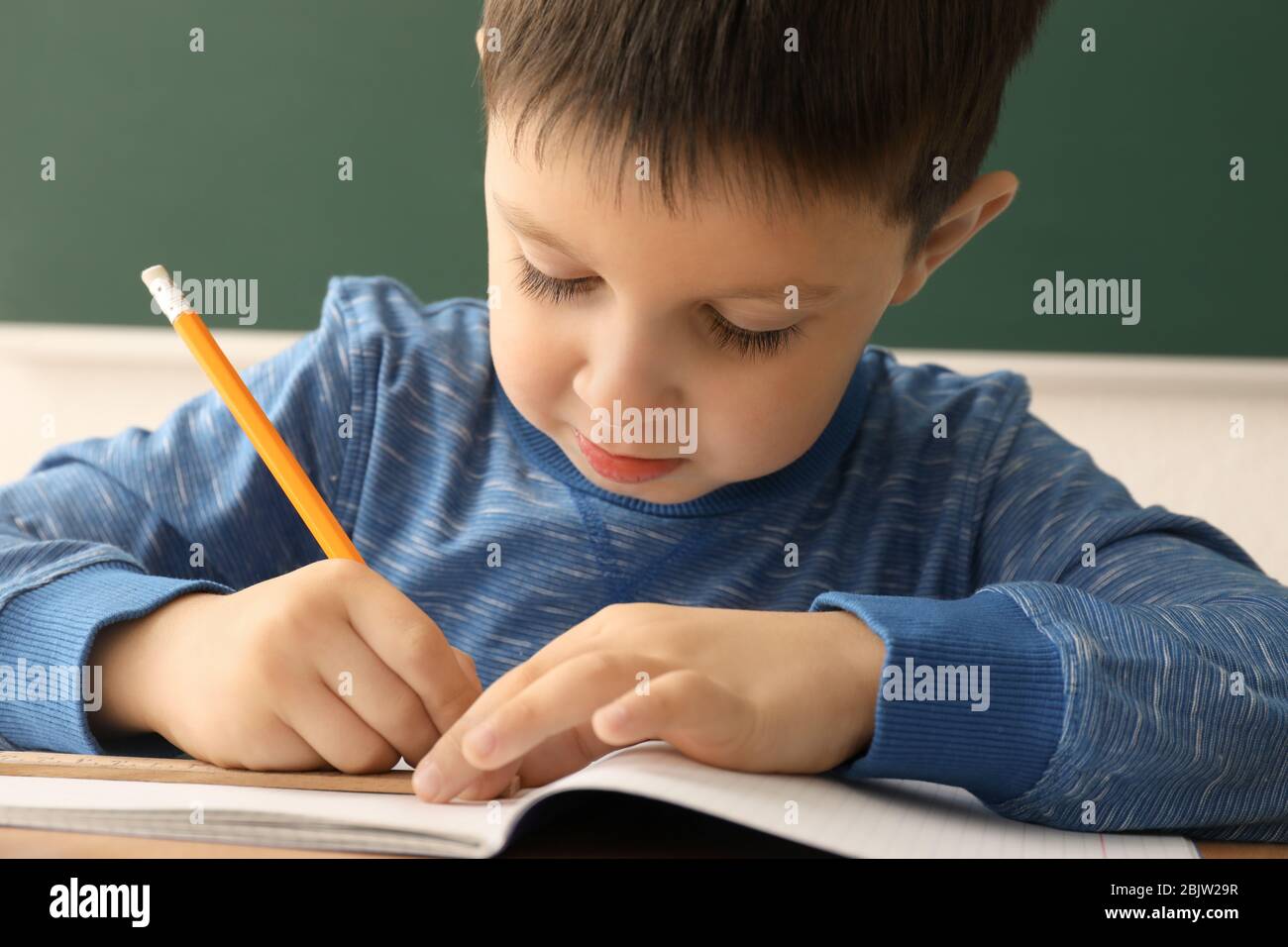 Cute little boy doing homework in classroom Stock Photo - Alamy