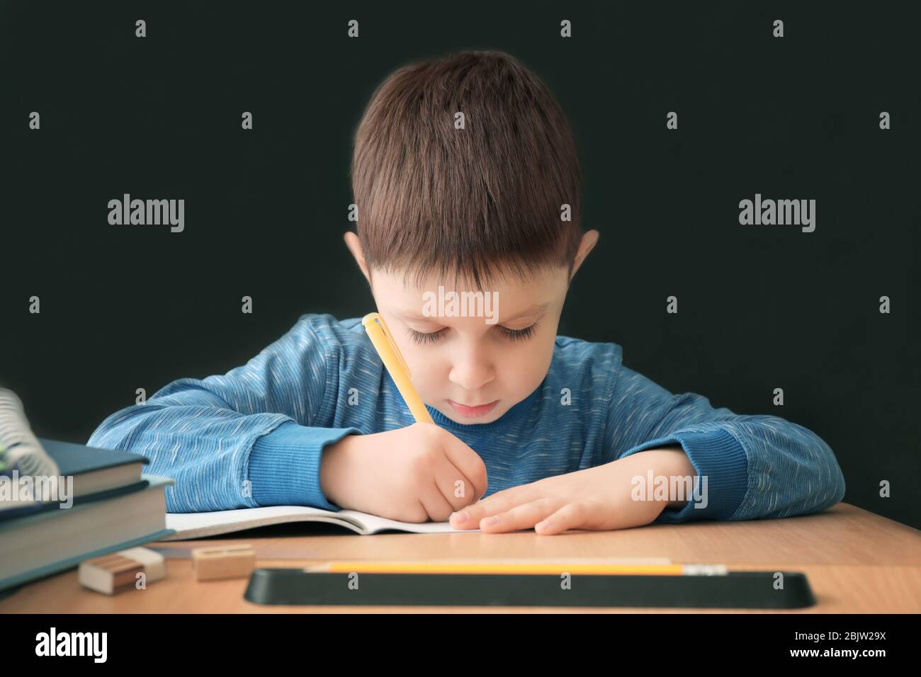 Cute little boy doing homework against black background Stock Photo - Alamy