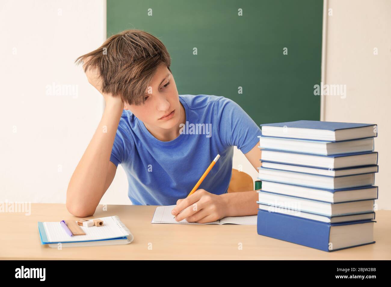 Tired teenager boy with lot of homework to do in classroom Stock Photo ...