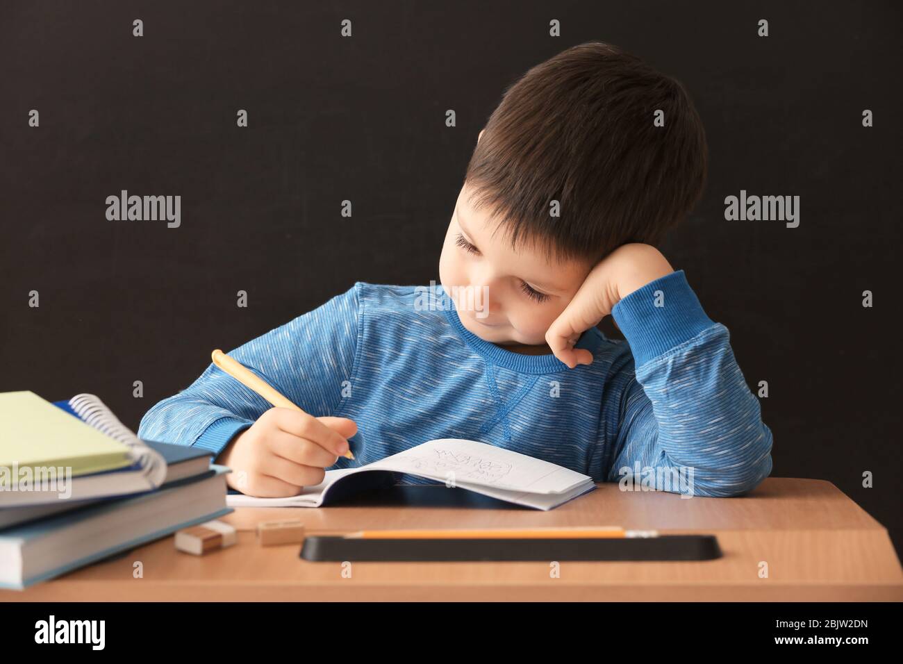 Cute little boy doing homework against black background Stock Photo - Alamy