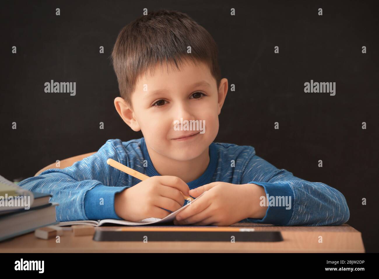 Cute little boy doing homework against black background Stock Photo - Alamy