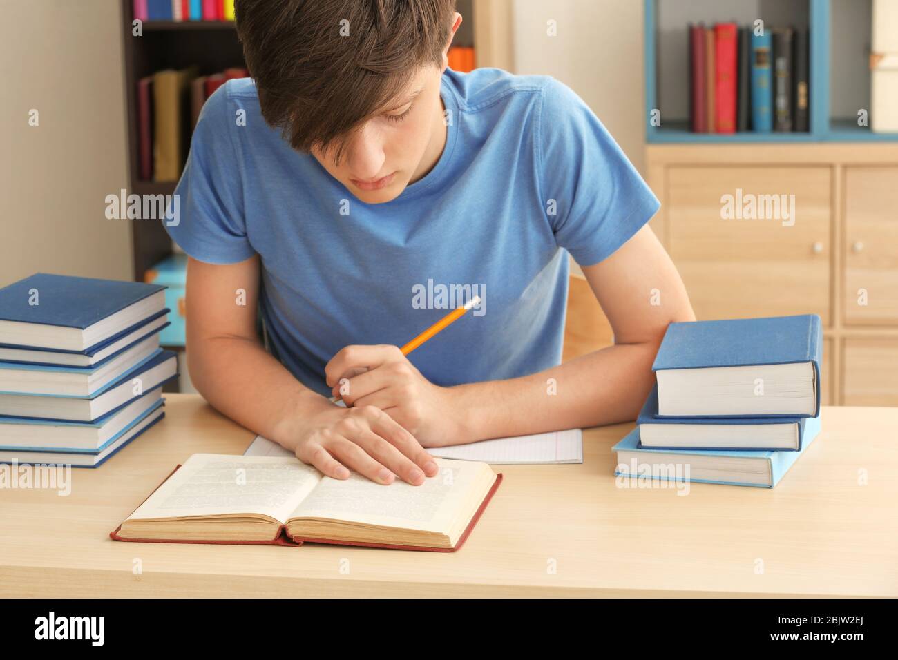 Cute teenager boy doing homework in library Stock Photo - Alamy
