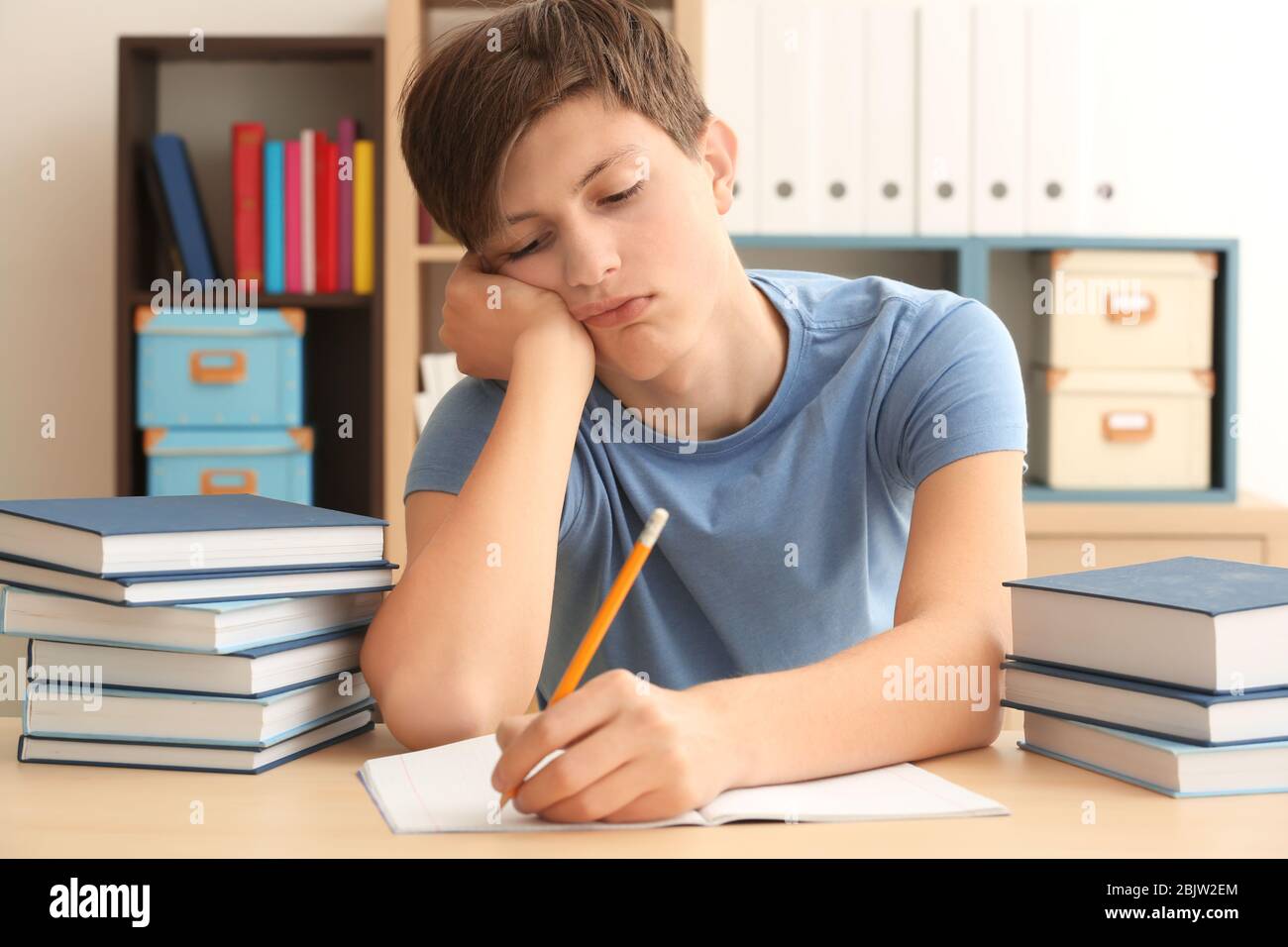 Tired teenager boy doing homework in library Stock Photo - Alamy