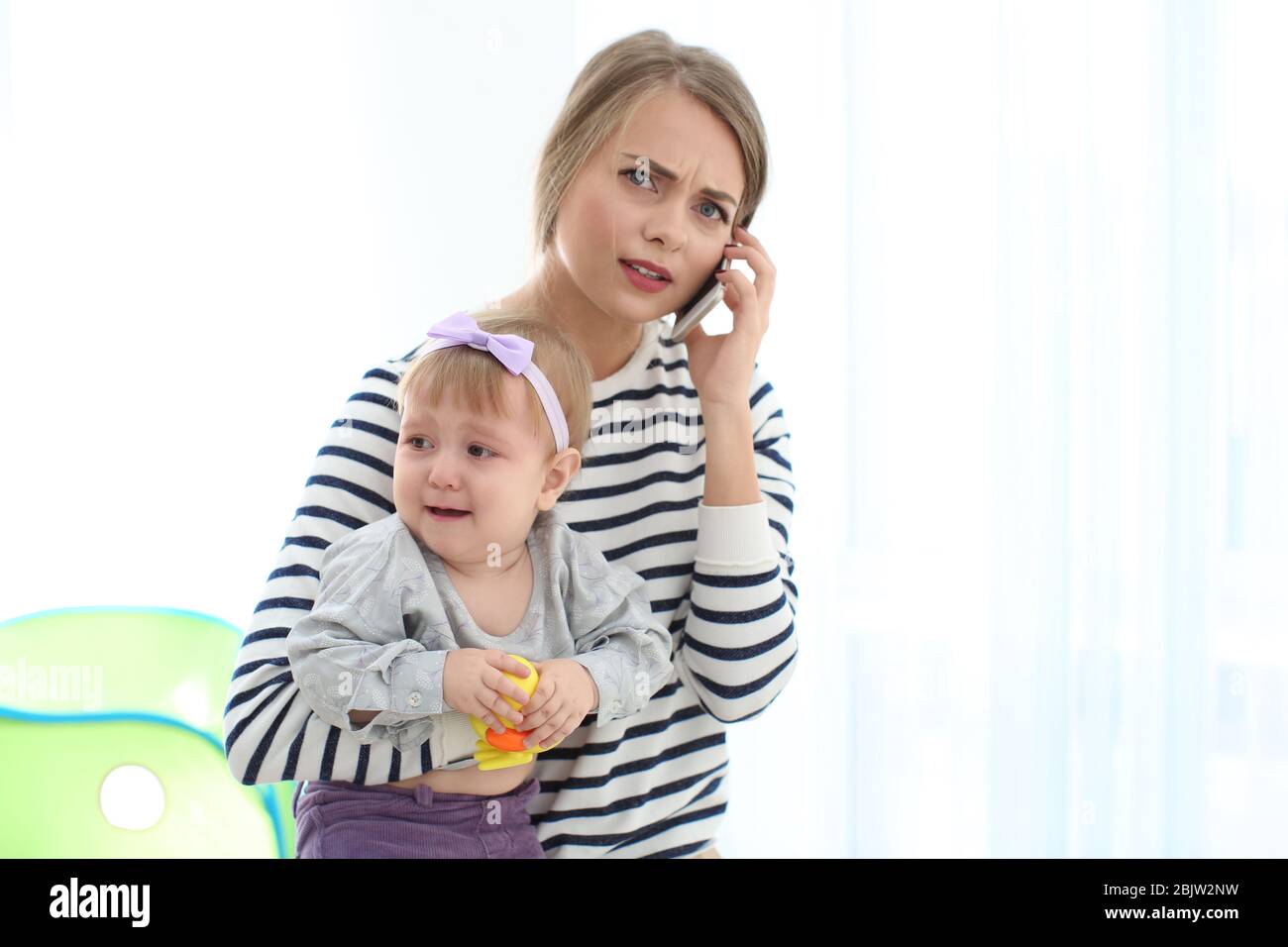 Young nanny holding girl while talking on mobile phone, indoors Stock ...