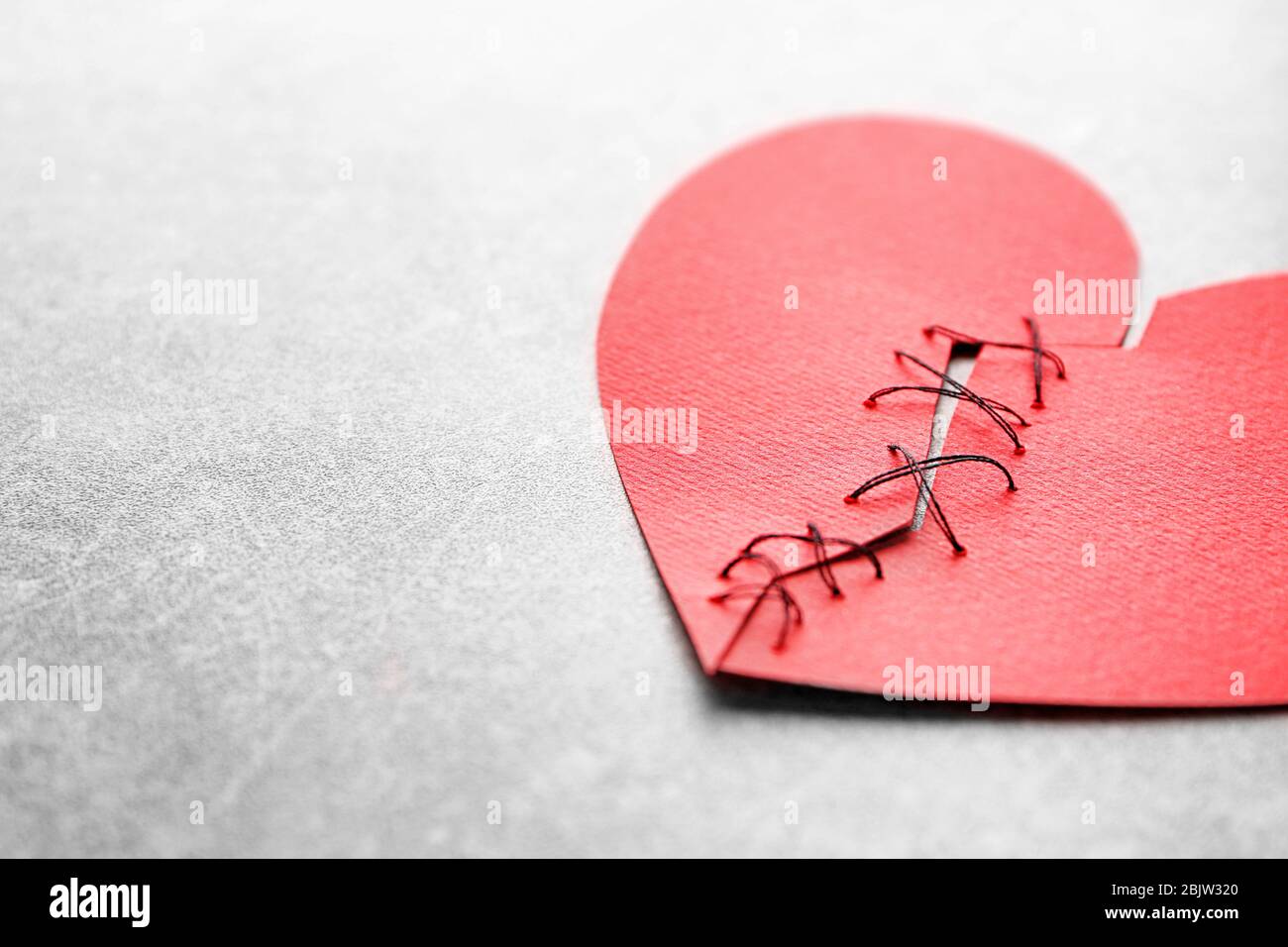 Paper heart cut in half and sewn back together on light background ...