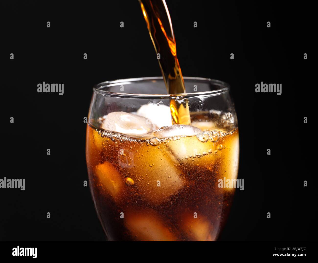 Pouring cola into glass with ice against black background, closeup ...
