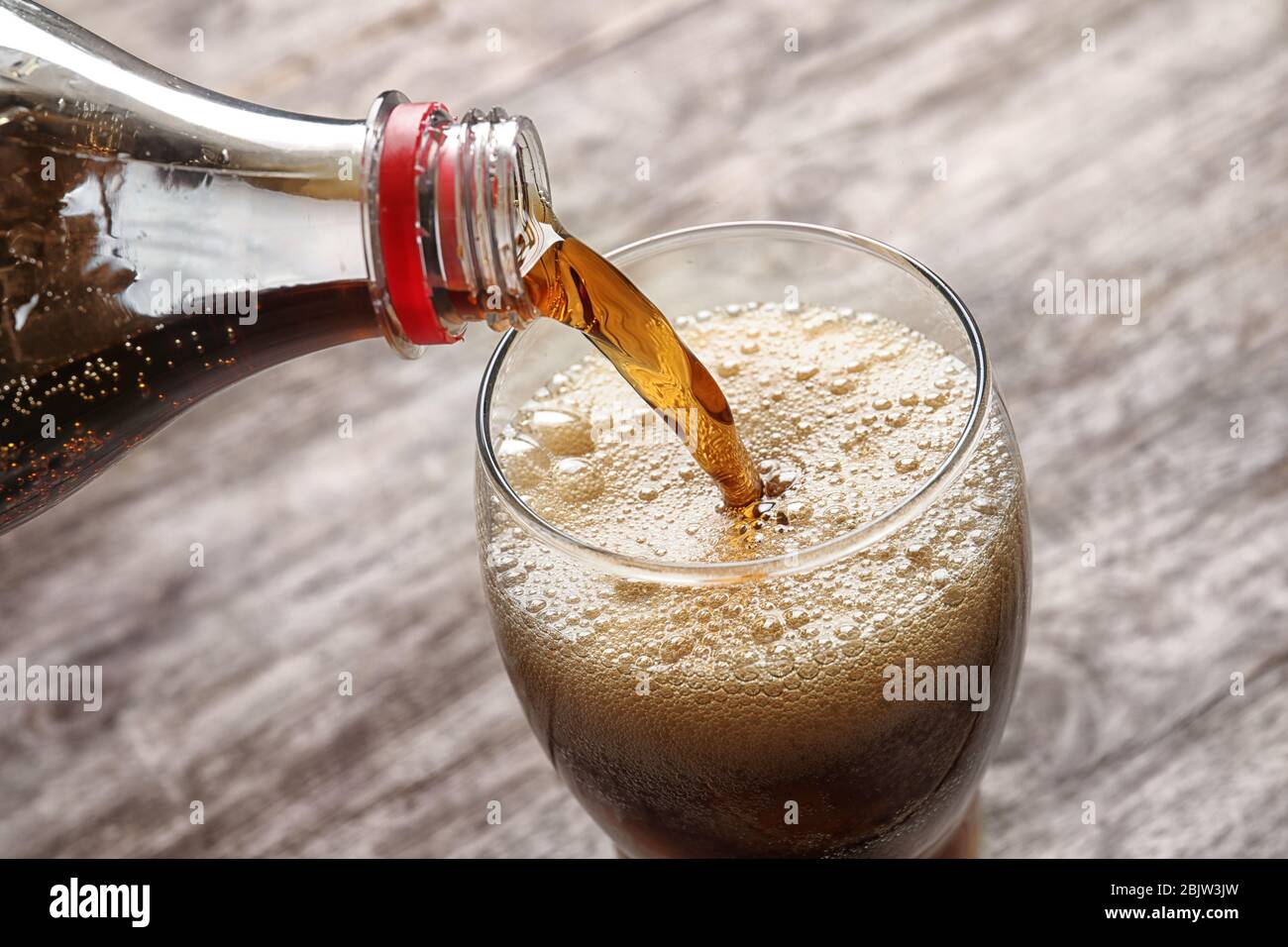 Pouring cola from bottle into glass on wooden background, closeup Stock ...