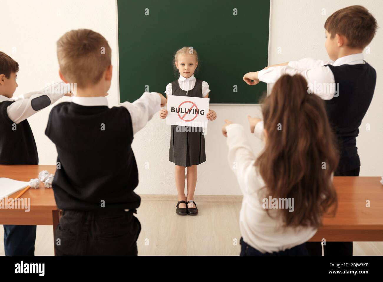 Little girl holding sign with crossed word "Bullying" in classroom ...