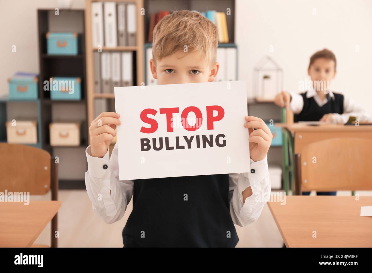 Little boy holding sign with words "Stop bullying" in classroom Stock ...