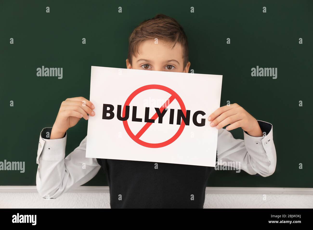 Little boy holding sign with crossed word "Bullying" in classroom Stock ...