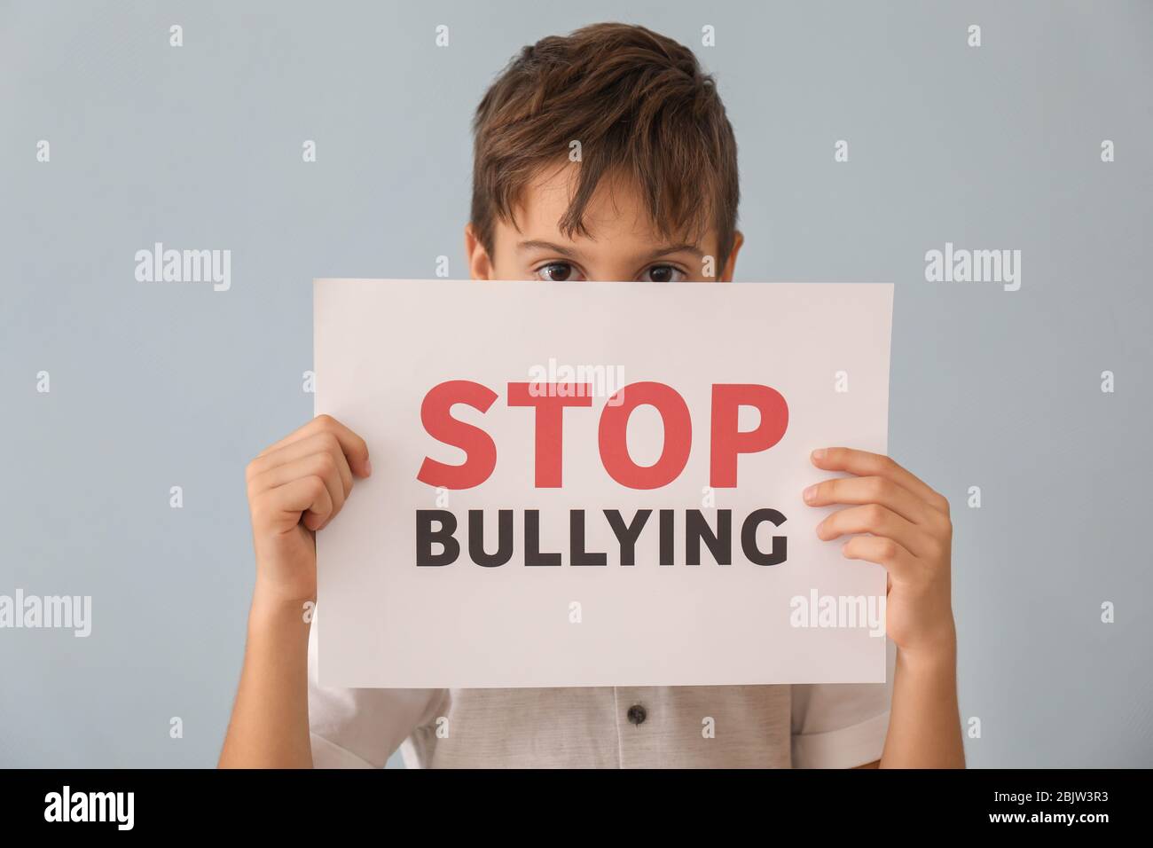 Little boy holding sign with words "Stop Bullying" on grey background ...