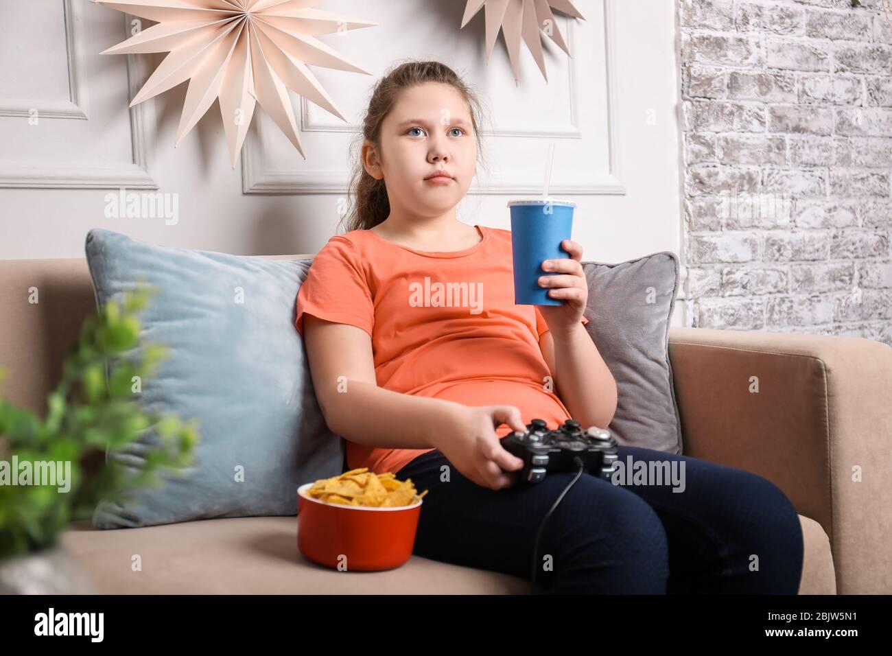Overweight girl playing videogame with snacks indoors Stock Photo - Alamy
