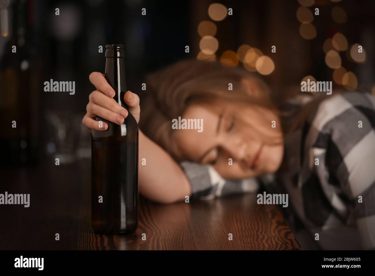 Unconscious drunk woman with bottle of drink in bar. Alcoholism problem ...