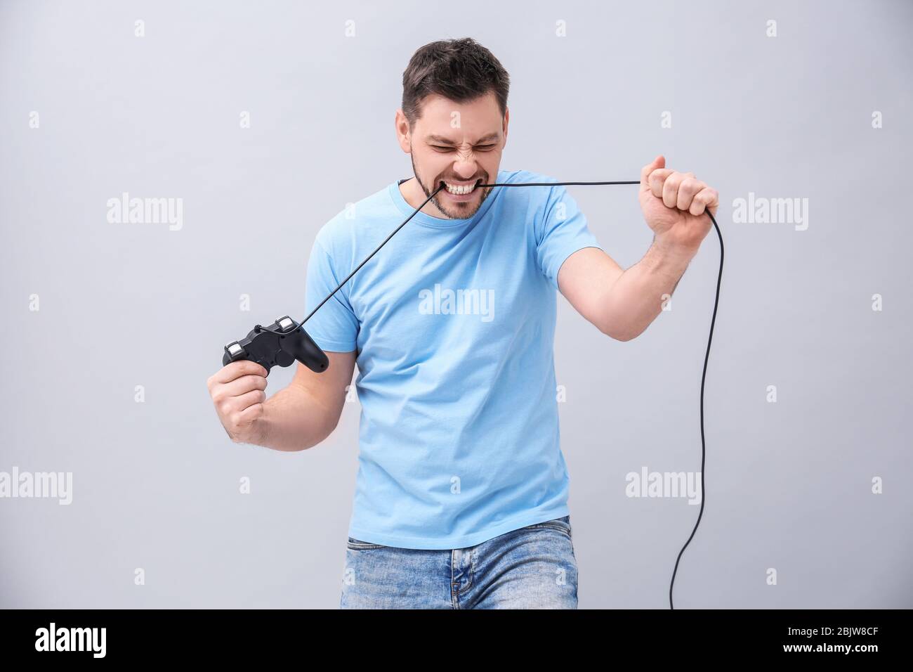 Angry man with video game controller on grey background Stock Photo - Alamy
