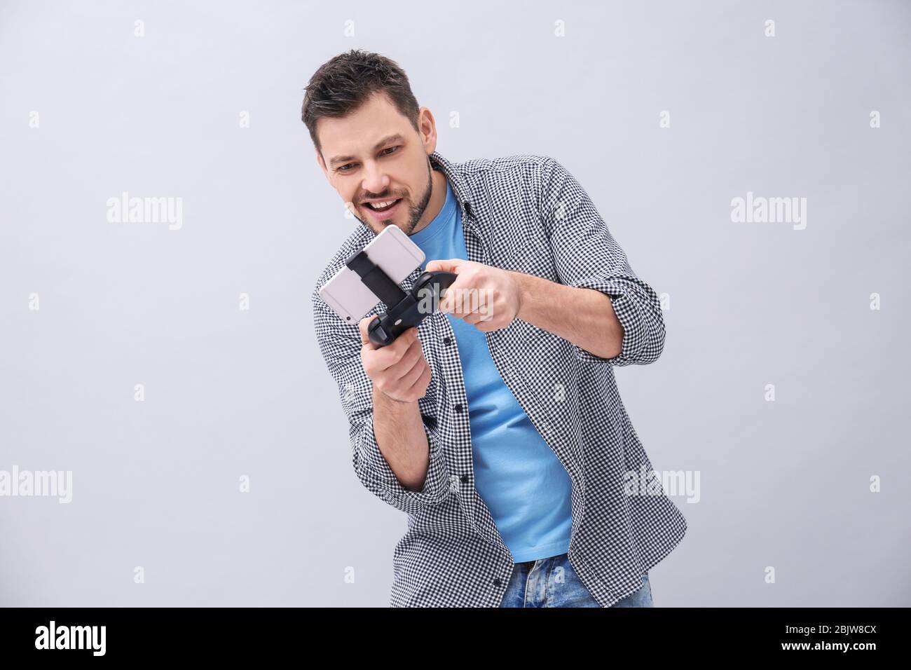 Emotional man with video game controller for smartphone on grey ...