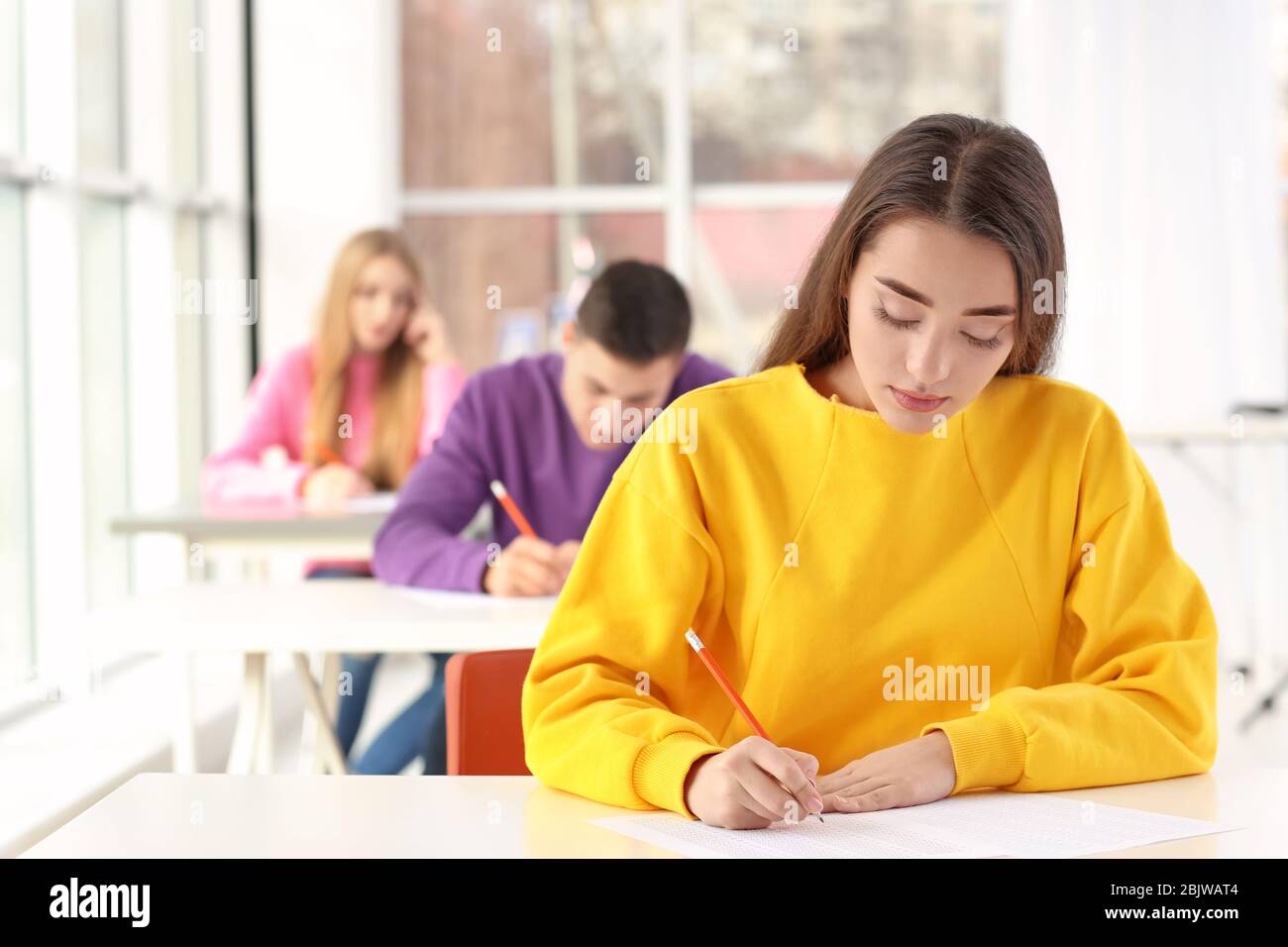 Student writing test to pass exam in classroom Stock Photo - Alamy