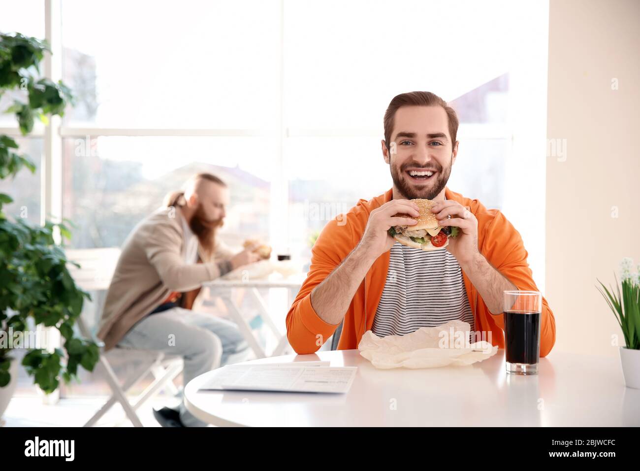 Handsome man eating yummy burger in cafe Stock Photo - Alamy