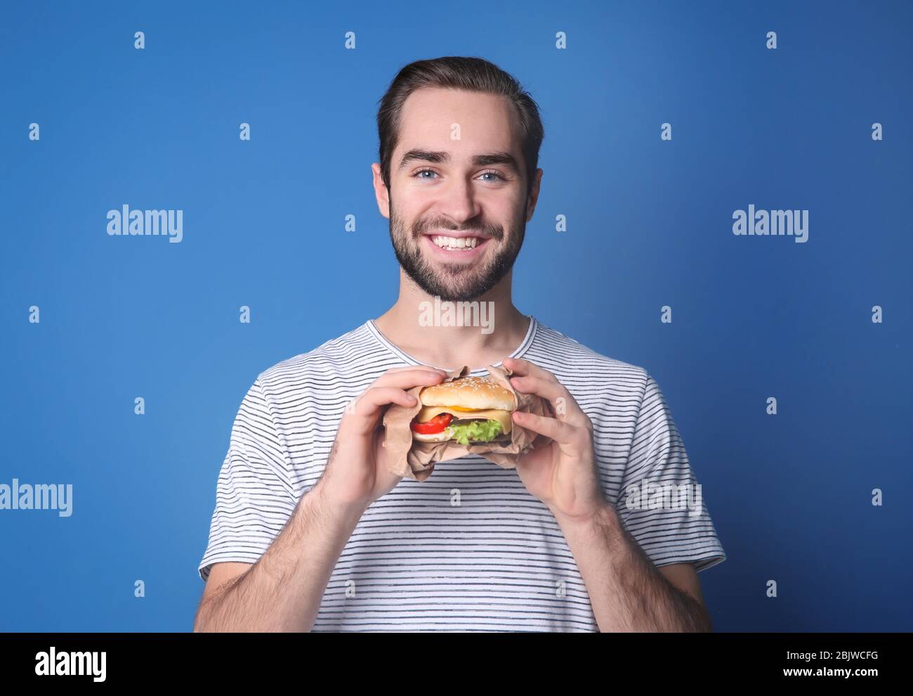 Handsome man with yummy burger against color background Stock Photo - Alamy