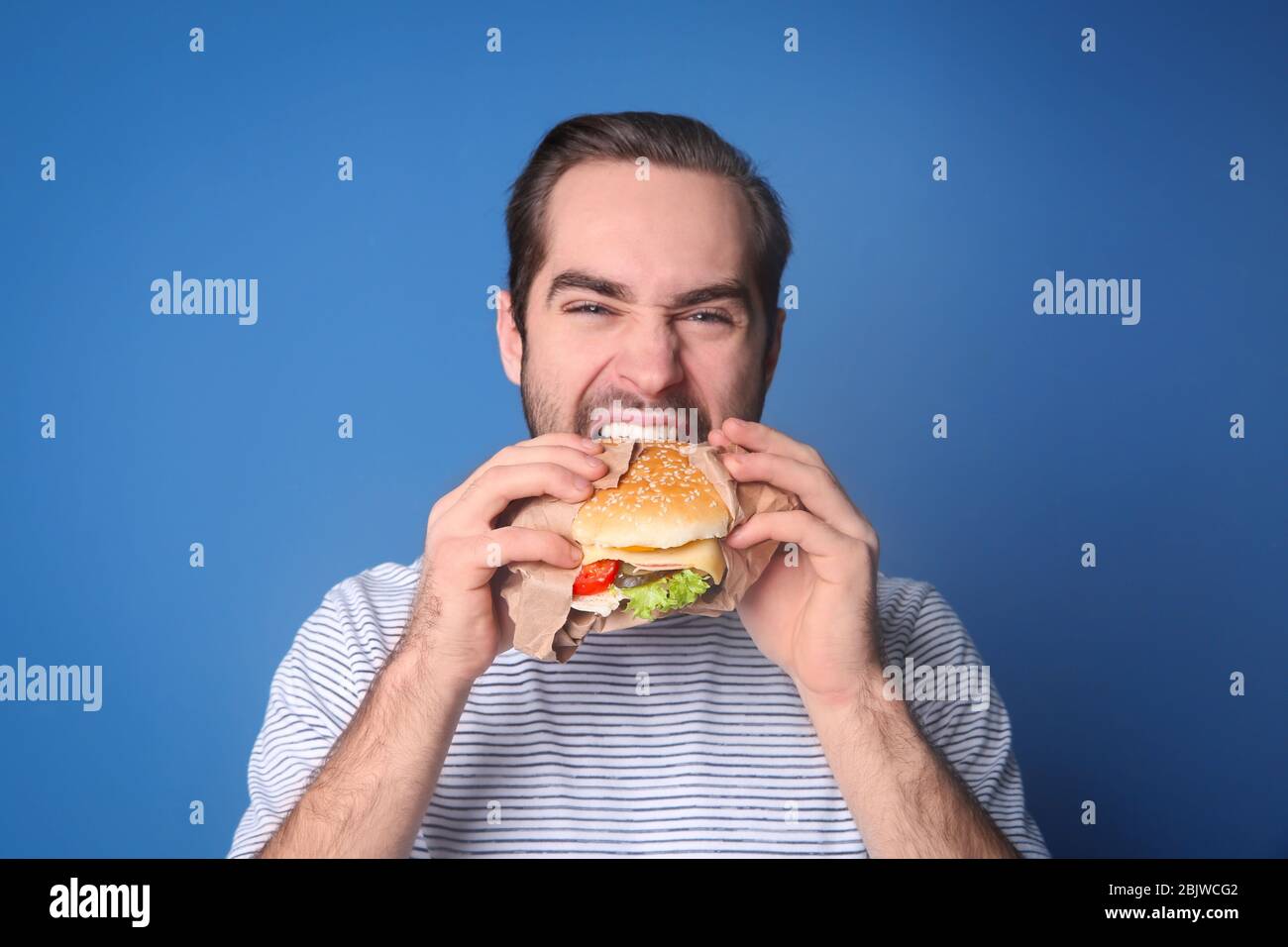 Handsome man eating yummy burger against color background Stock Photo ...