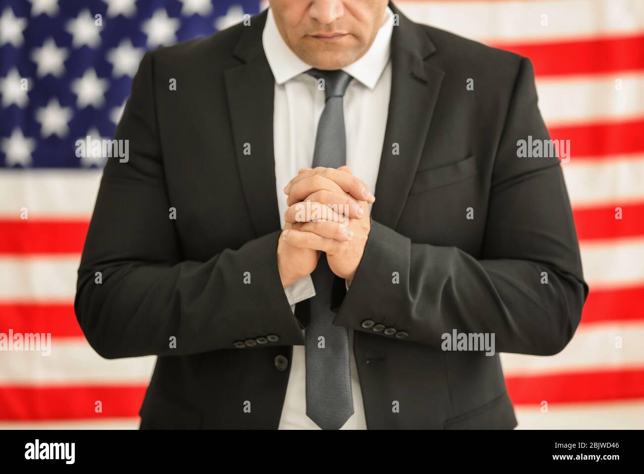 Man in suit praying on American flag background Stock Photo - Alamy