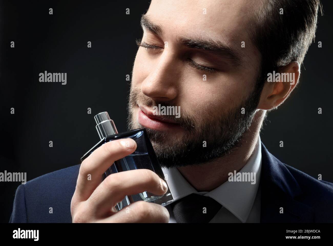 Handsome man in formal suit and with bottle of perfume on dark ...