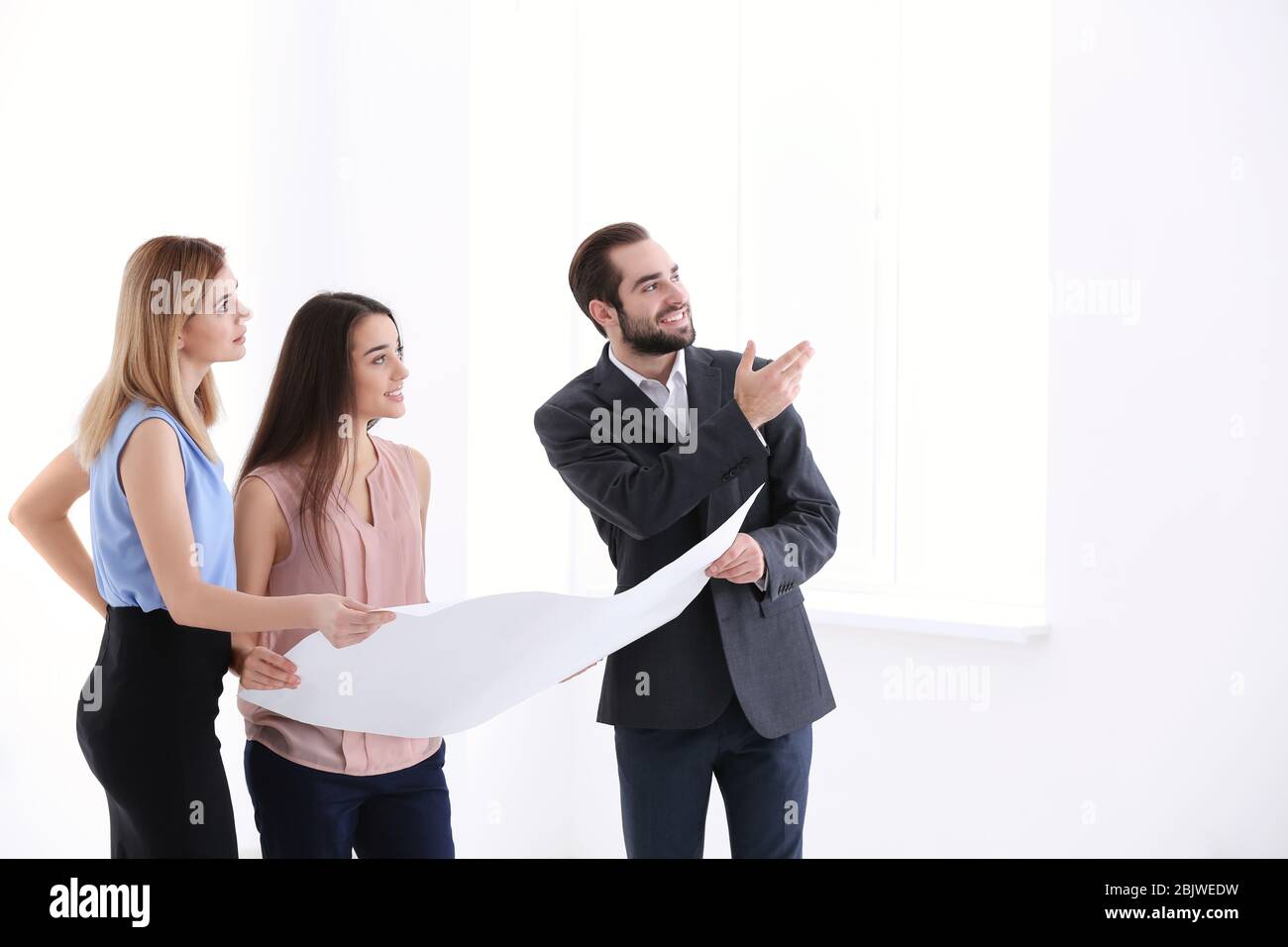 Real estate agent with trainee showing plan of apartment to client ...